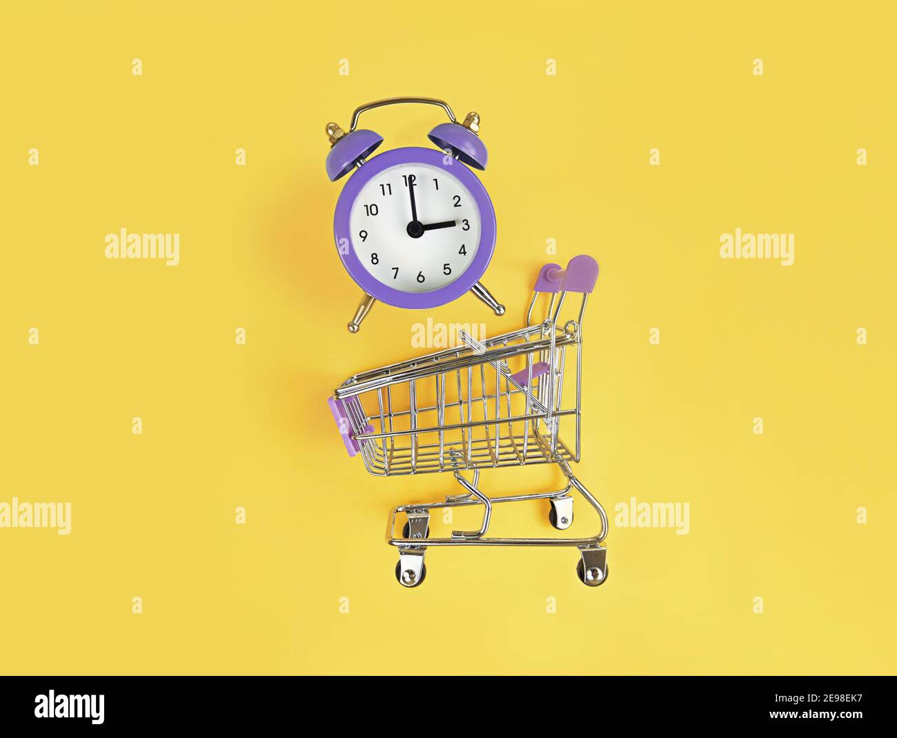 Supermarket trolley and violet alarm clock on yellow background. Buy ...