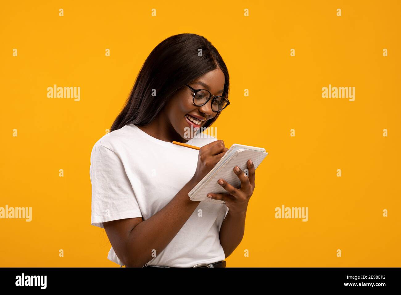 Intelligent black woman in glasses student taking notes on yellow Stock ...