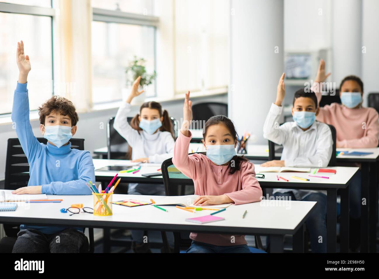Schoolchildren raising hands at classroom, wearing medical masks Stock ...