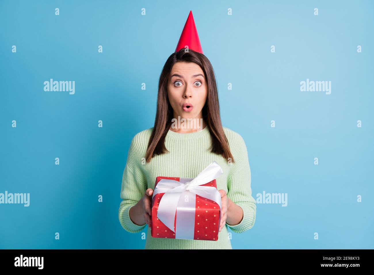 Photo portrait of shocked girl holding box wearing red birthday hat ...