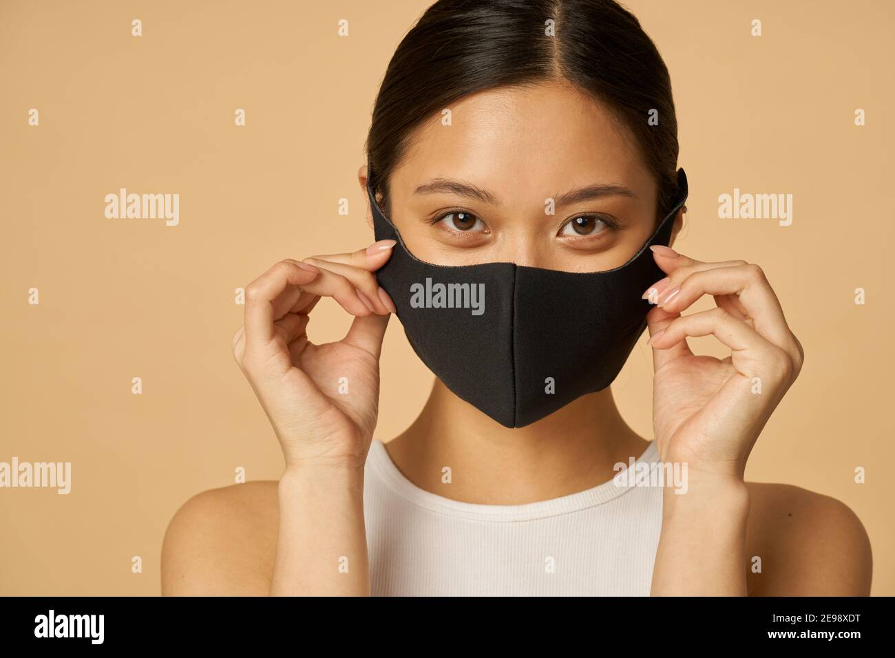Charming young woman adjusting black facial mask and looking at camera ...