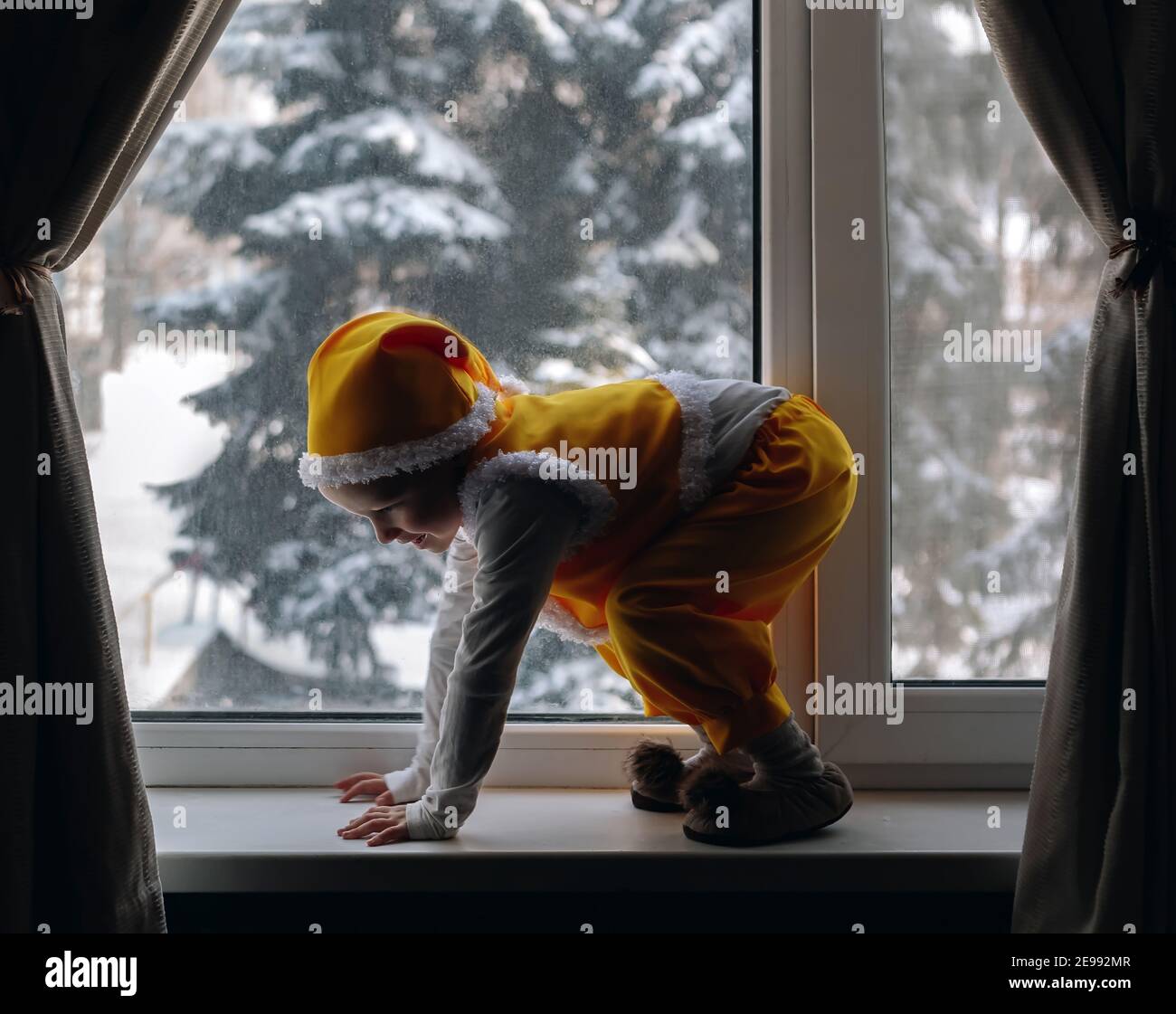 Little boy 4 years old play at window with winter view wear yellow ...