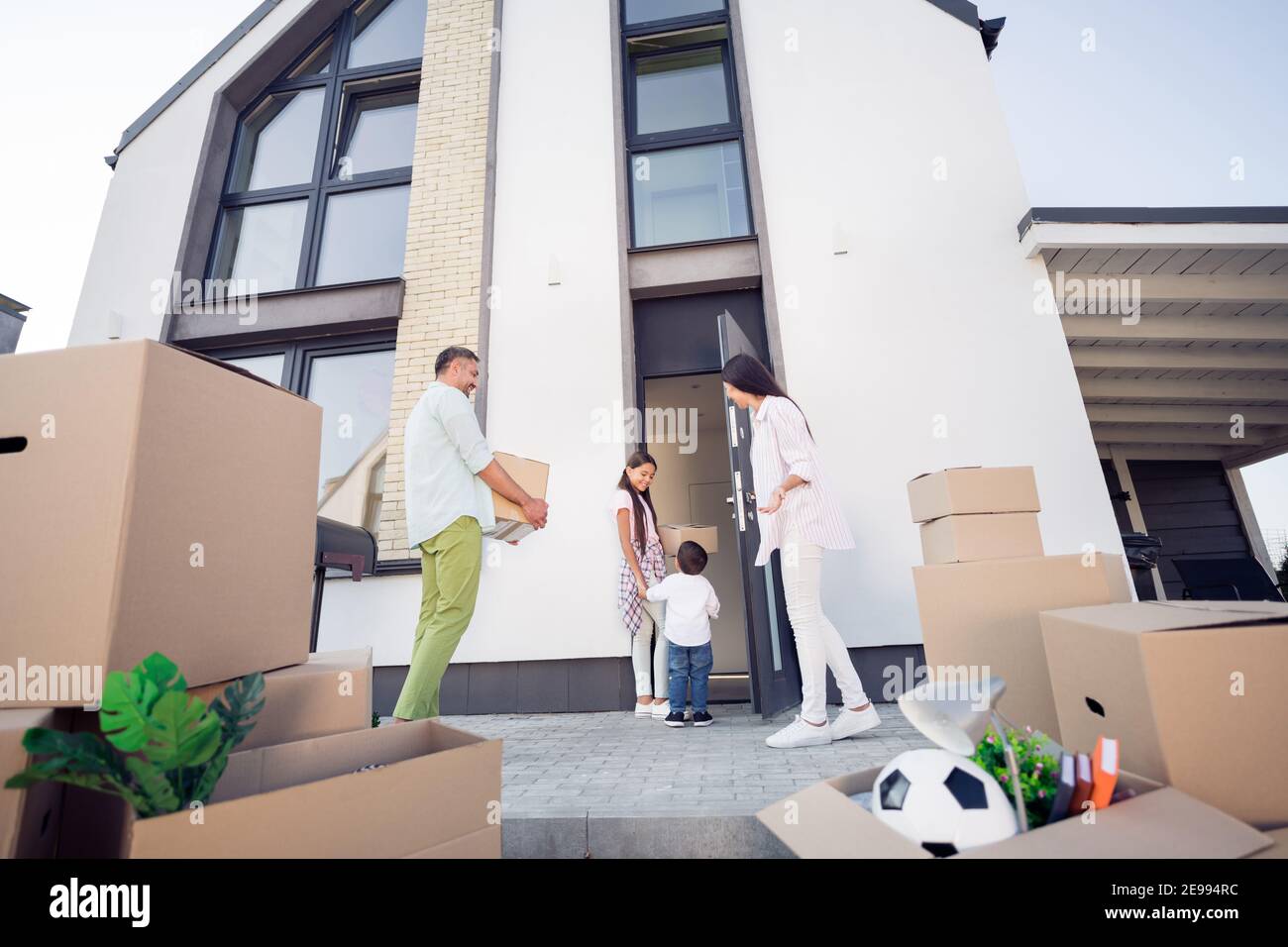 Photo portrait of happy family of four moving to new home carrying ...