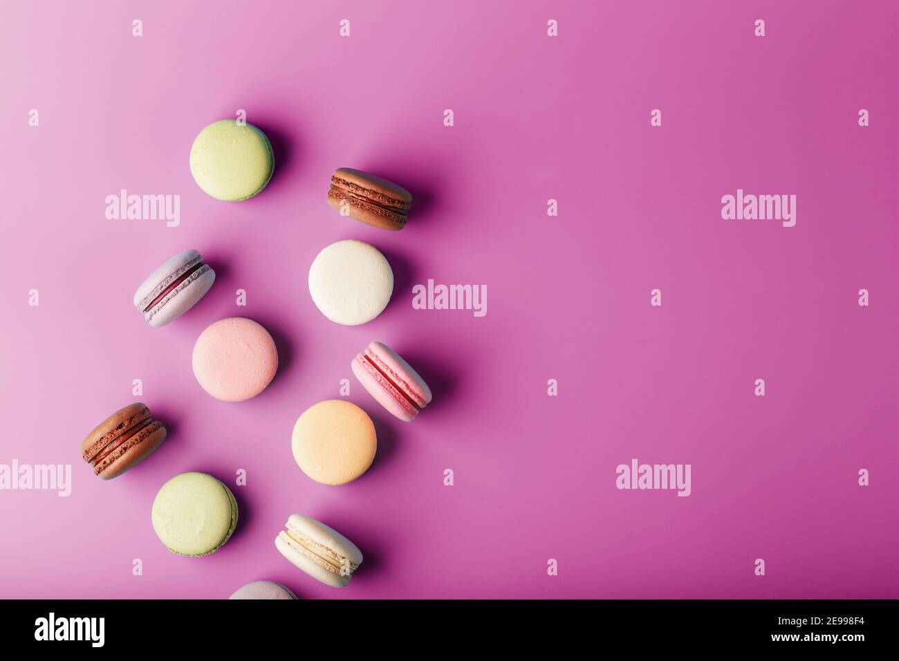 Colorful French macaroni cookies are scattered on a pink background ...