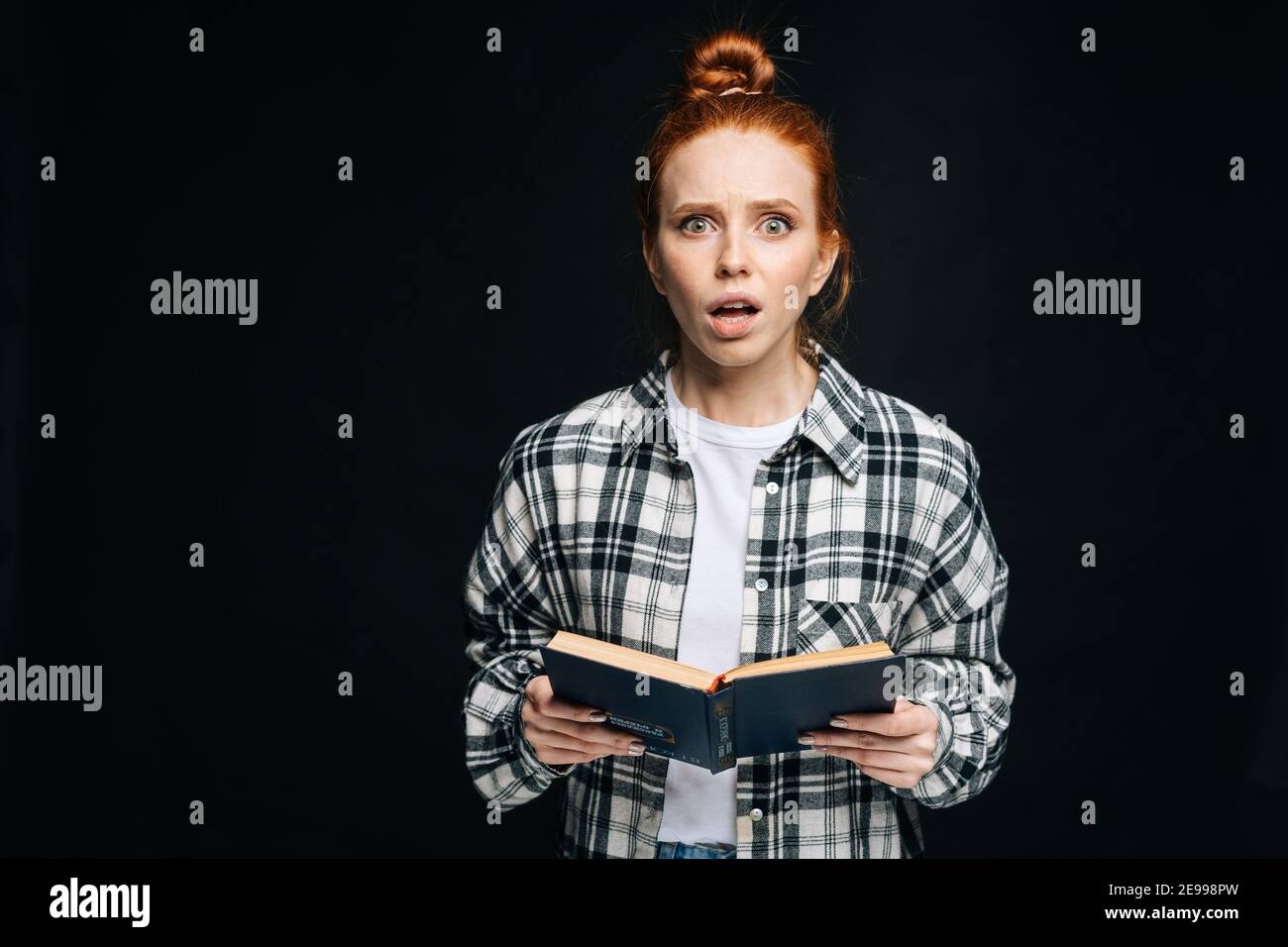 Shocked young woman college student with opened mouth holding books and ...