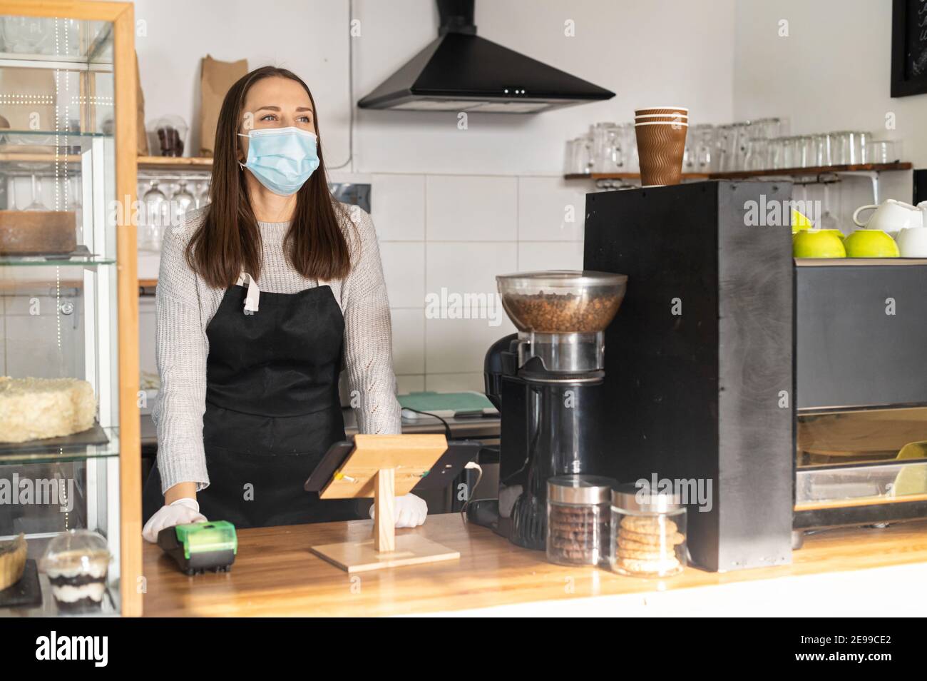 A female cafe owner wearing mask stands behind countertop and looking ...