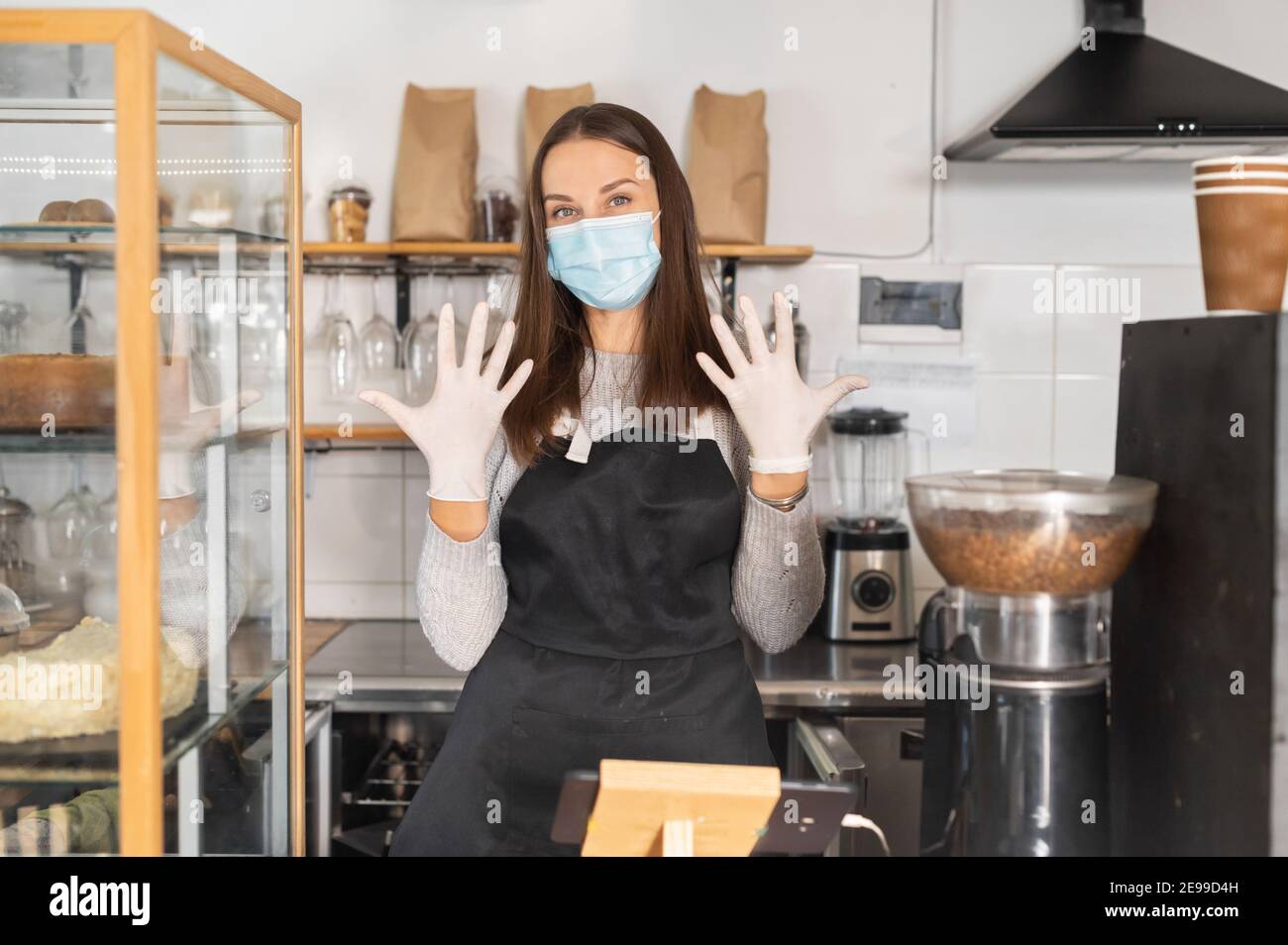 A waitress wearing protective mask shows at camera her hands in rubber ...