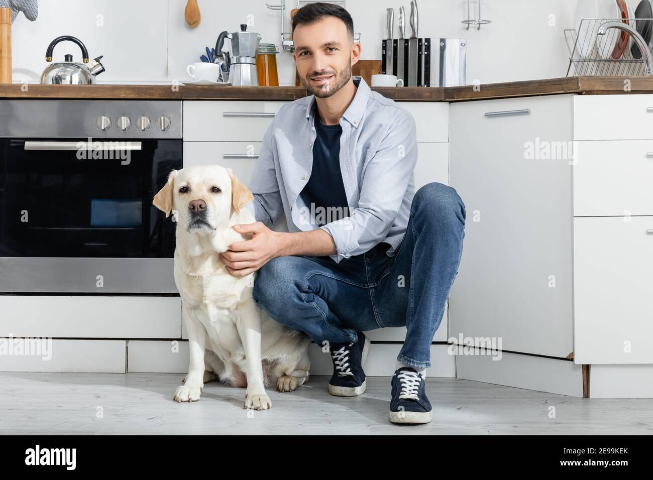 happy man in jeans sitting and cuddling labrador at home Stock Photo ...