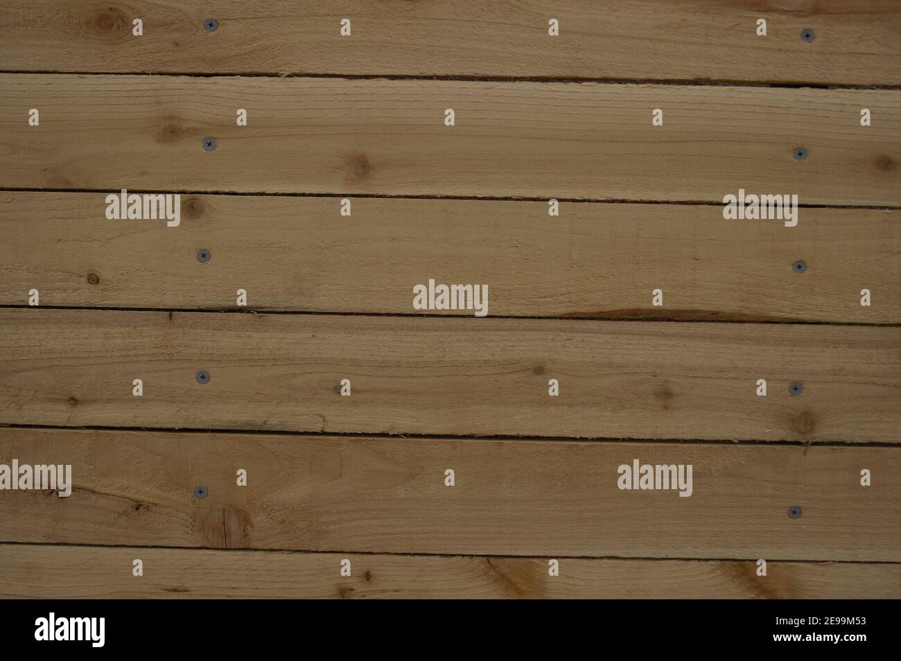 Horizontal pine boards are nailed together to construct a wall at a ...