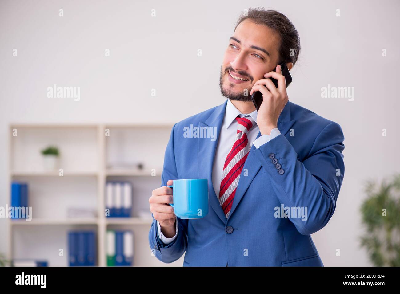 Young employee drinking coffee at workplace Stock Photo - Alamy