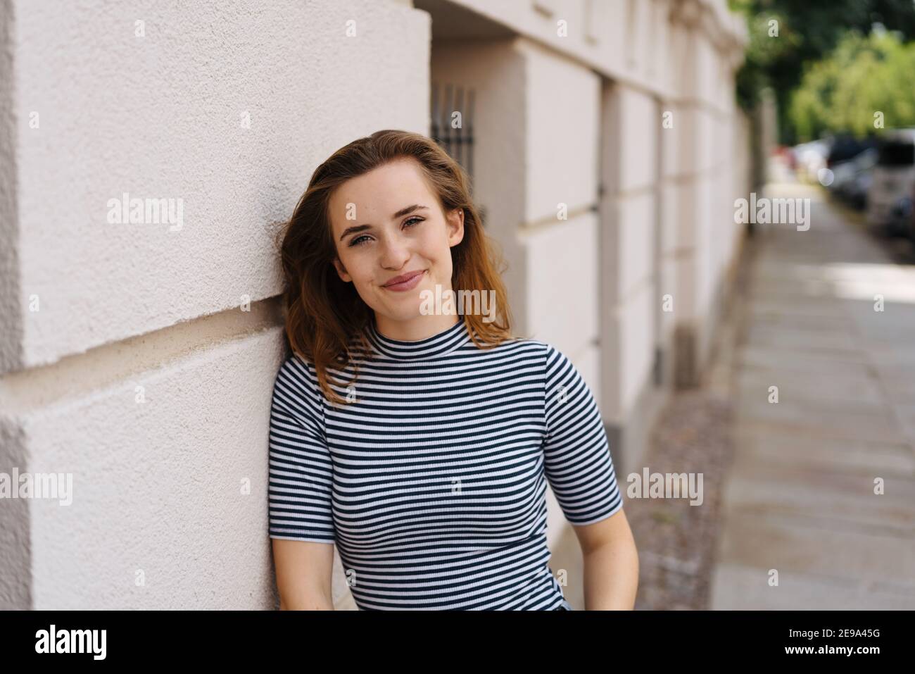 Attractive young woman with a sweet genuine smile standing leaning ...