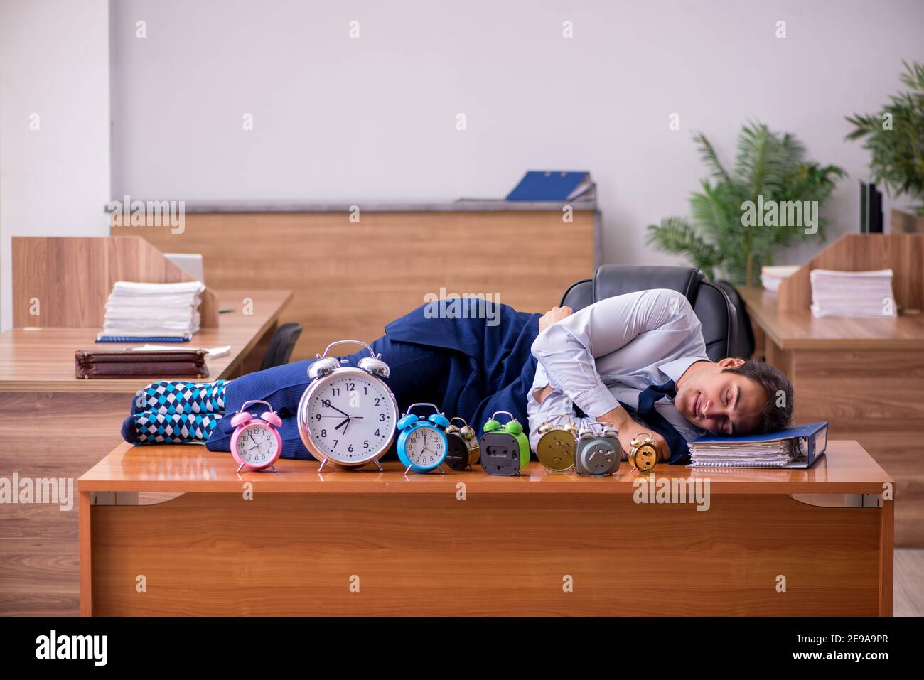 Young businessman sleeping in the office in time management concept ...