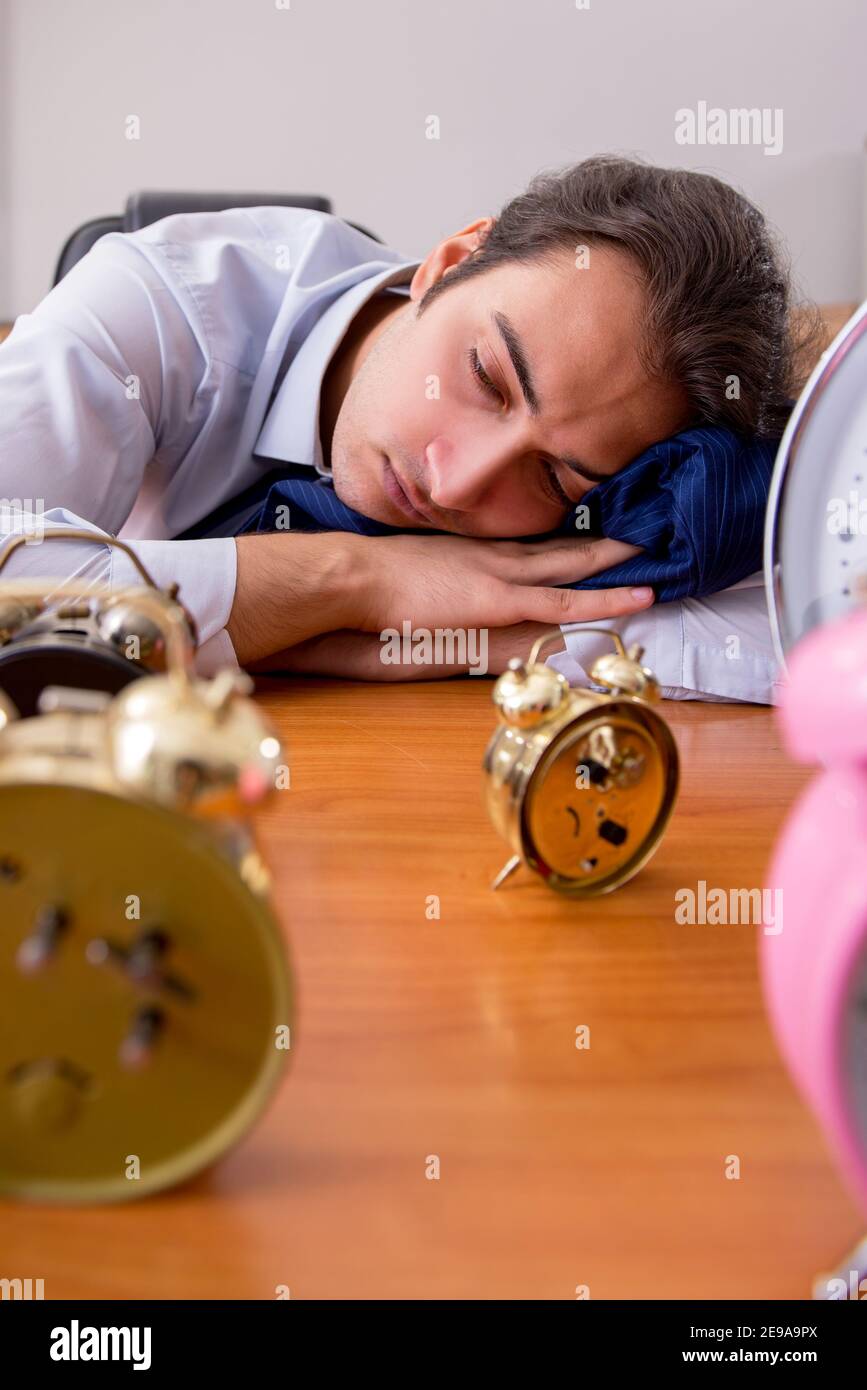 Young businessman sleeping in the office in time management concept ...