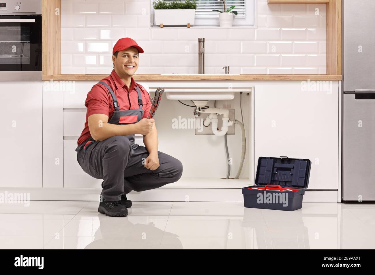 Plumber with a tool box kneeling next to a sink in a modern kitchen ...
