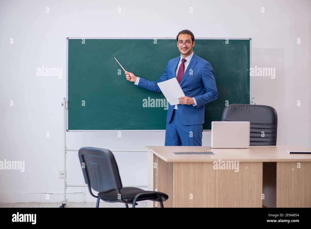 Young teacher in suit in front of green board Stock Photo - Alamy