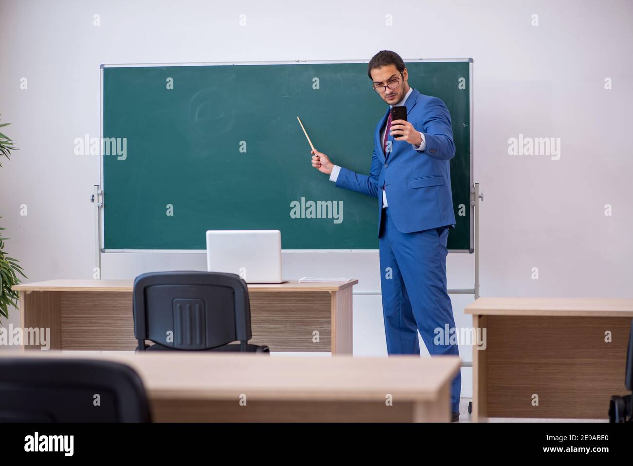 Young teacher in suit in front of green board Stock Photo - Alamy
