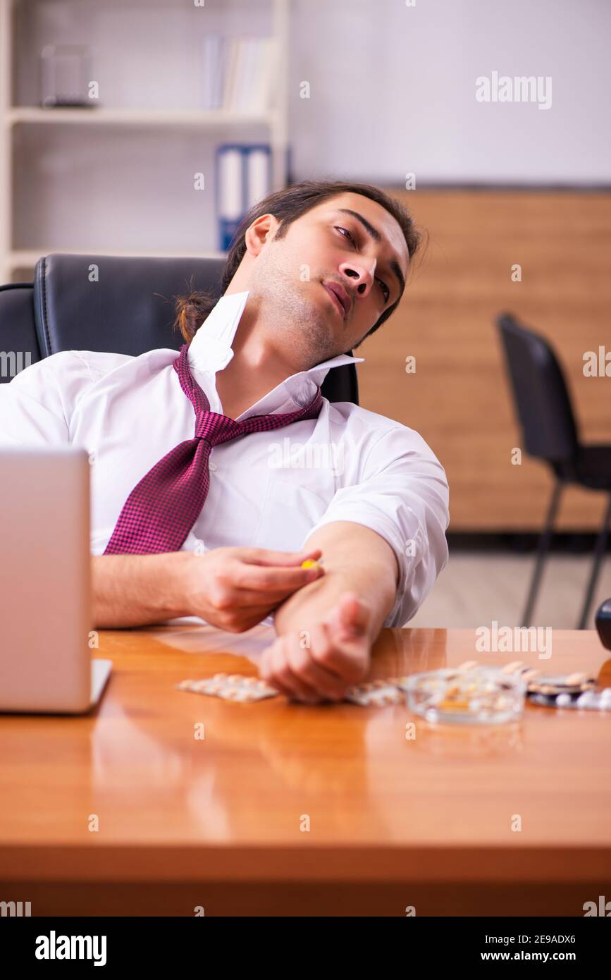 Young drug addicted male employee sitting at workplace Stock Photo - Alamy