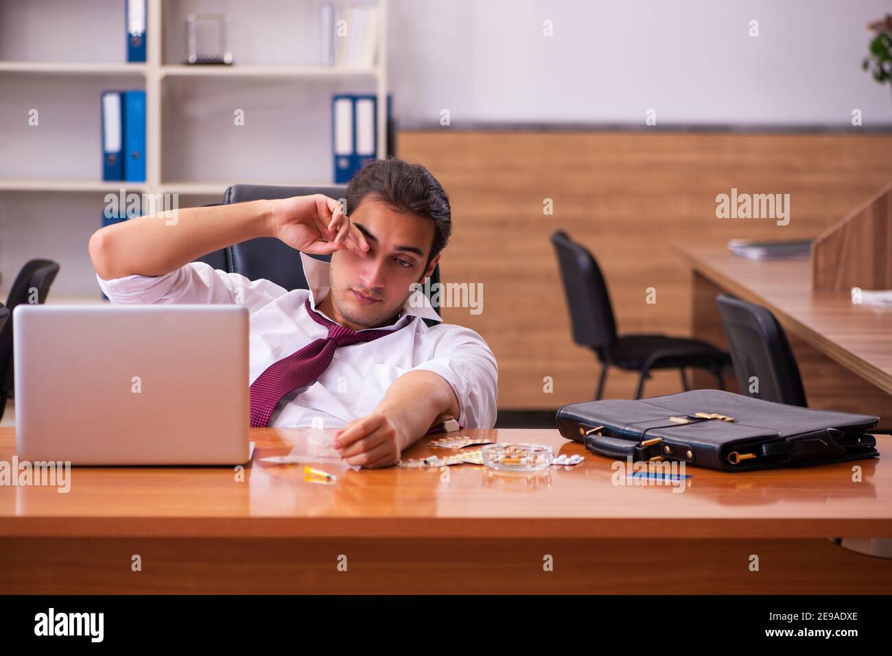 Young drug addicted male employee sitting at workplace Stock Photo - Alamy