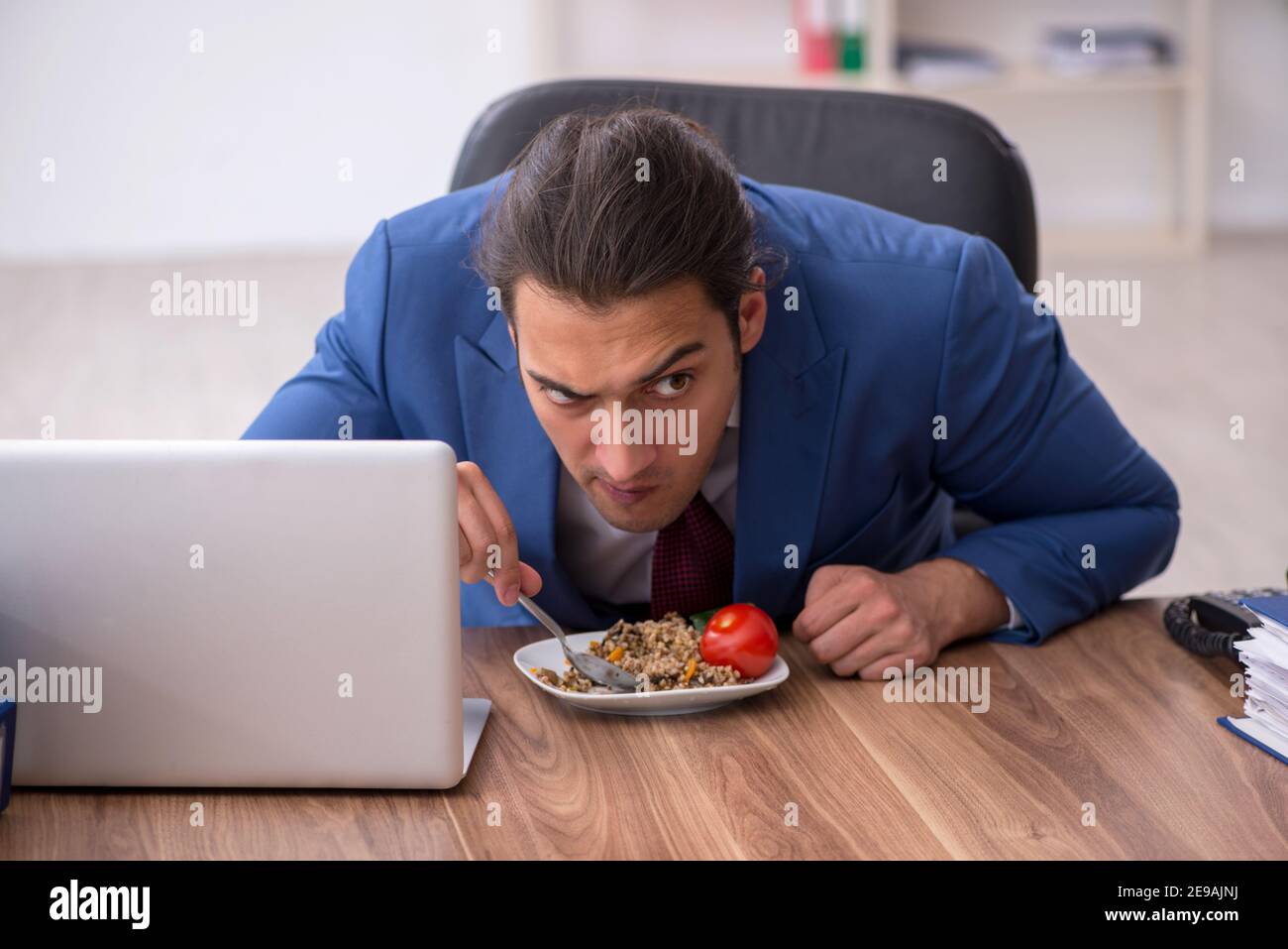 Hungry employee eating buckwheat during break Stock Photo - Alamy