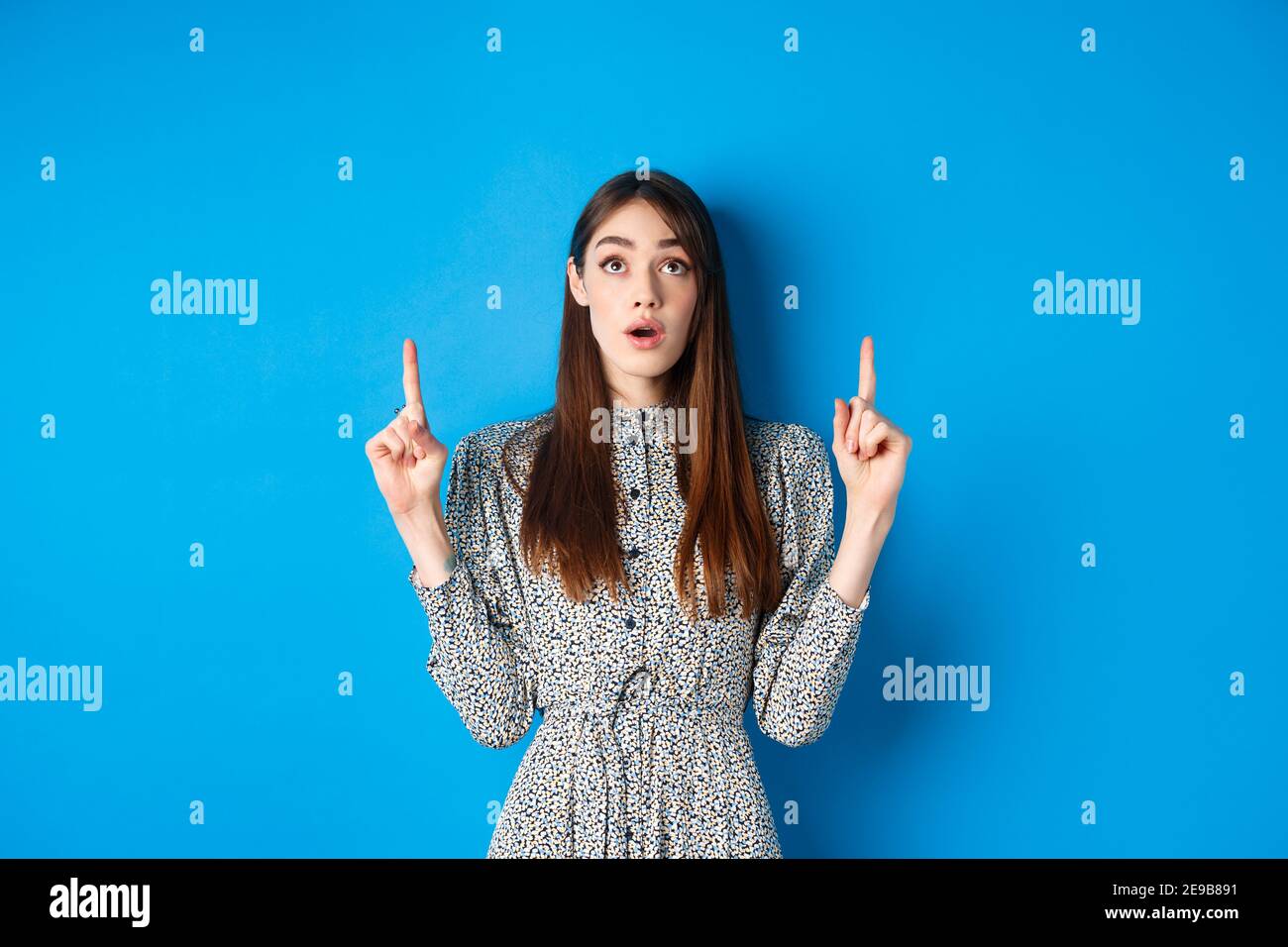 Surprised romantic girl in dress pointing, looking up with opened mouth ...