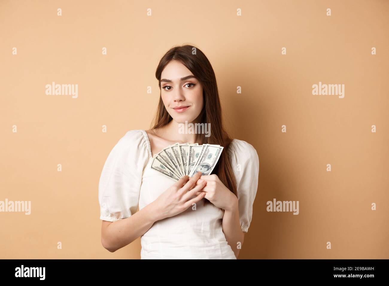 Smiling rich woman showing dollar bills and looking happy at camera ...