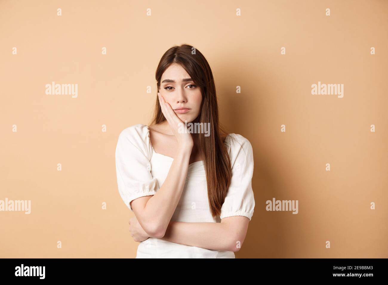 Bored and tired young woman looking indifferent at camera, lean face on ...