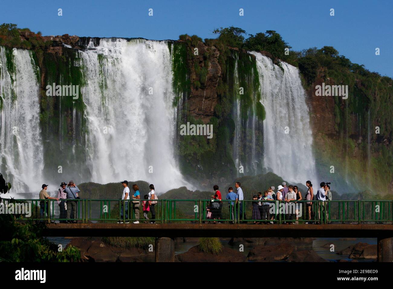 Tourists standing on a raised walkway admire a section of Iguazu Falls ...