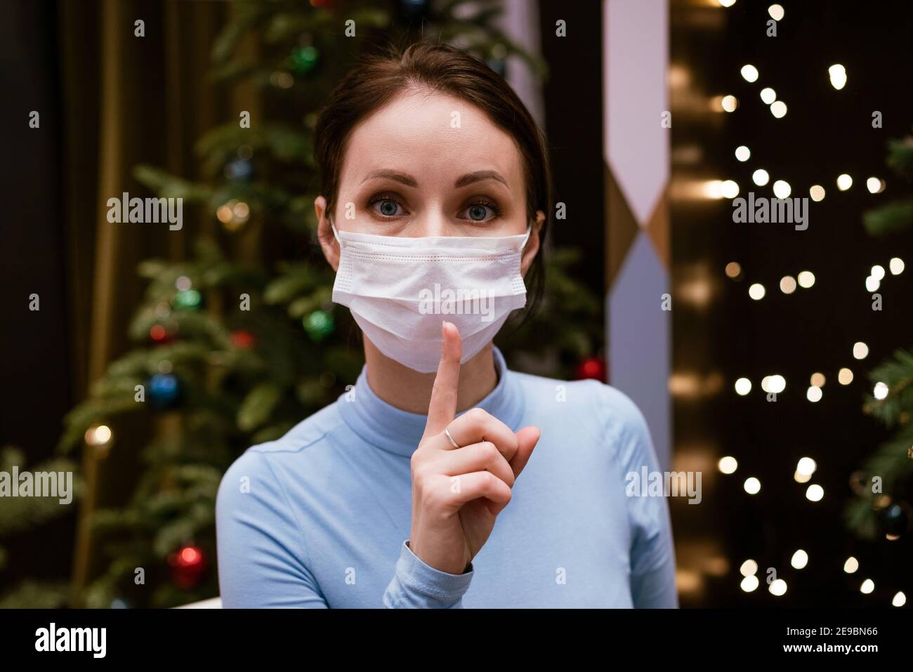 woman in medical mask shows finger gesture to be quiet on bokeh ...