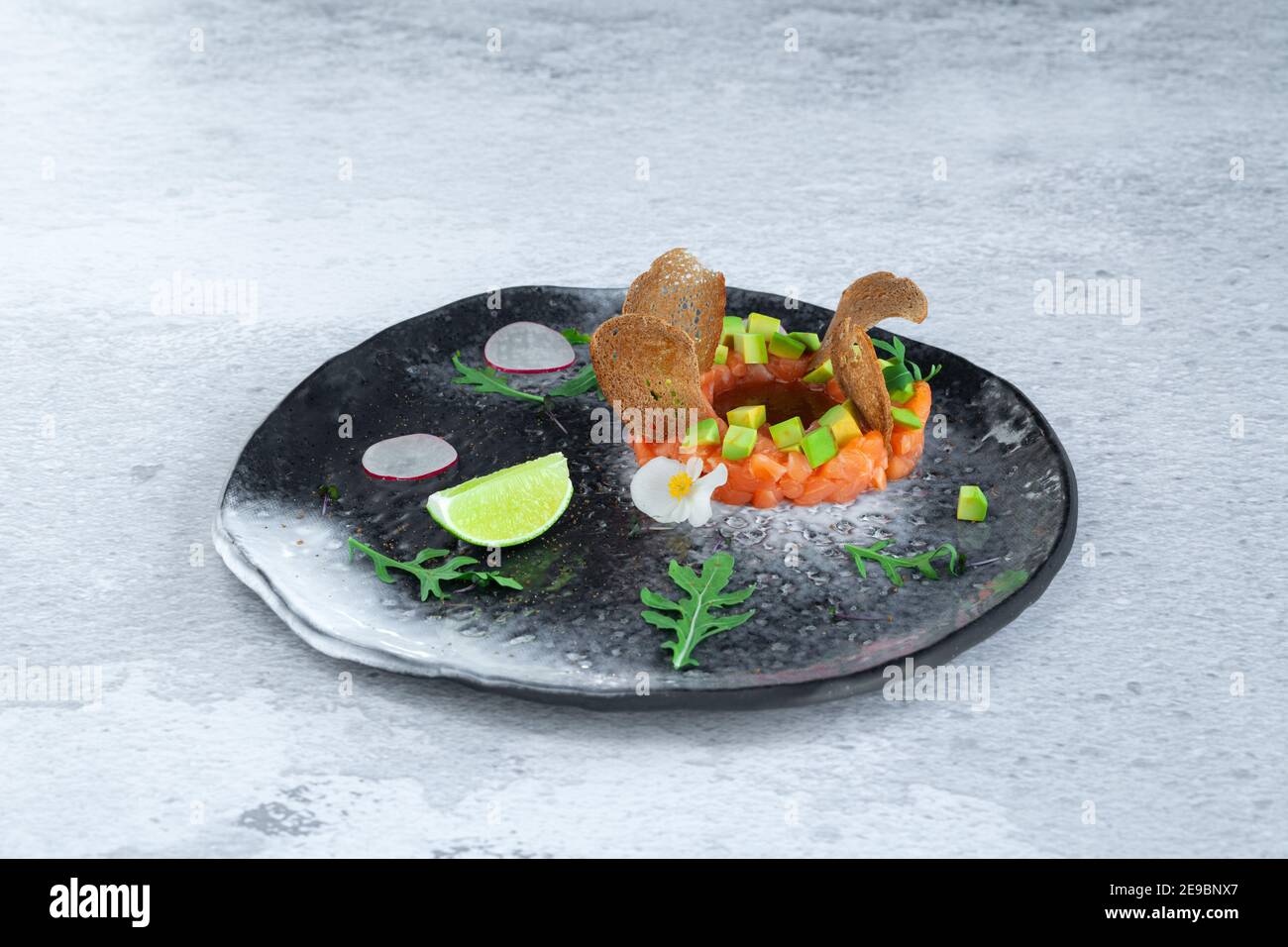 Portion of fresh salmon and avocado tartar on black plate Stock Photo ...