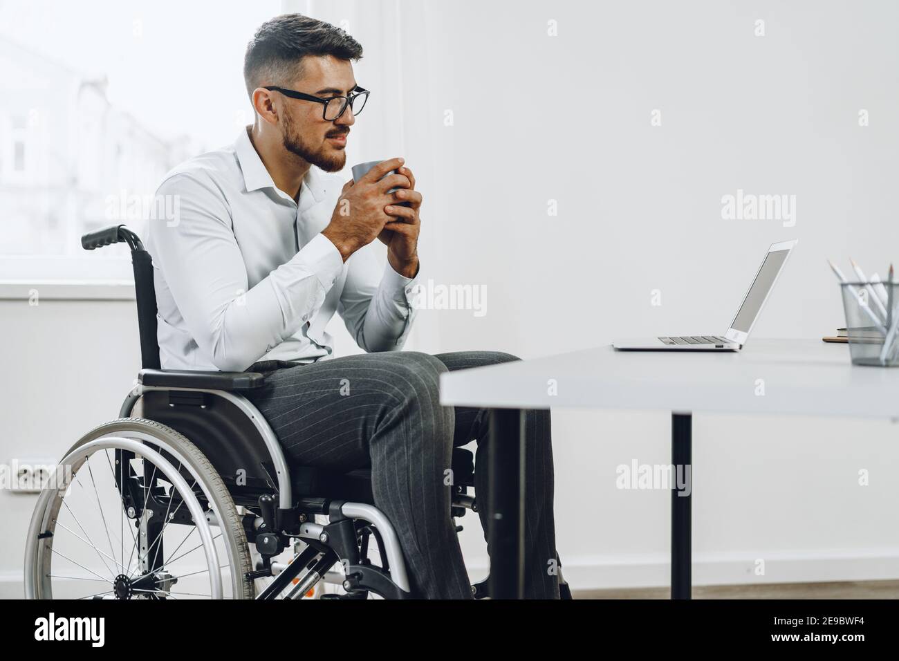 Positive disabled young man in wheelchair working in office Stock Photo ...