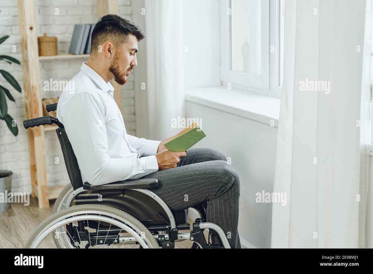 Disabled man in wheelchair reading a book indoors Stock Photo - Alamy
