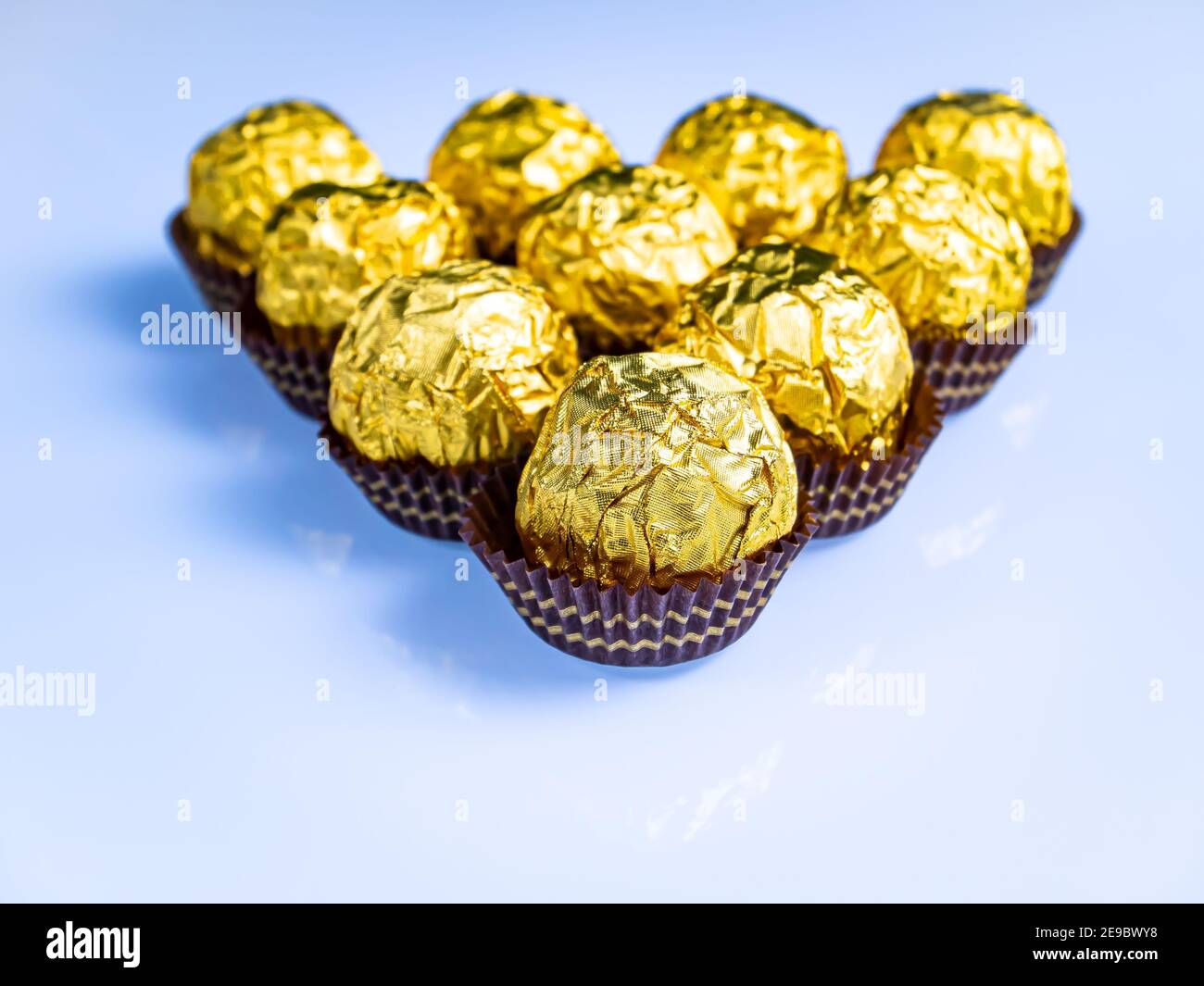Round chocolate candies in a golden foil wrapper on a white background ...