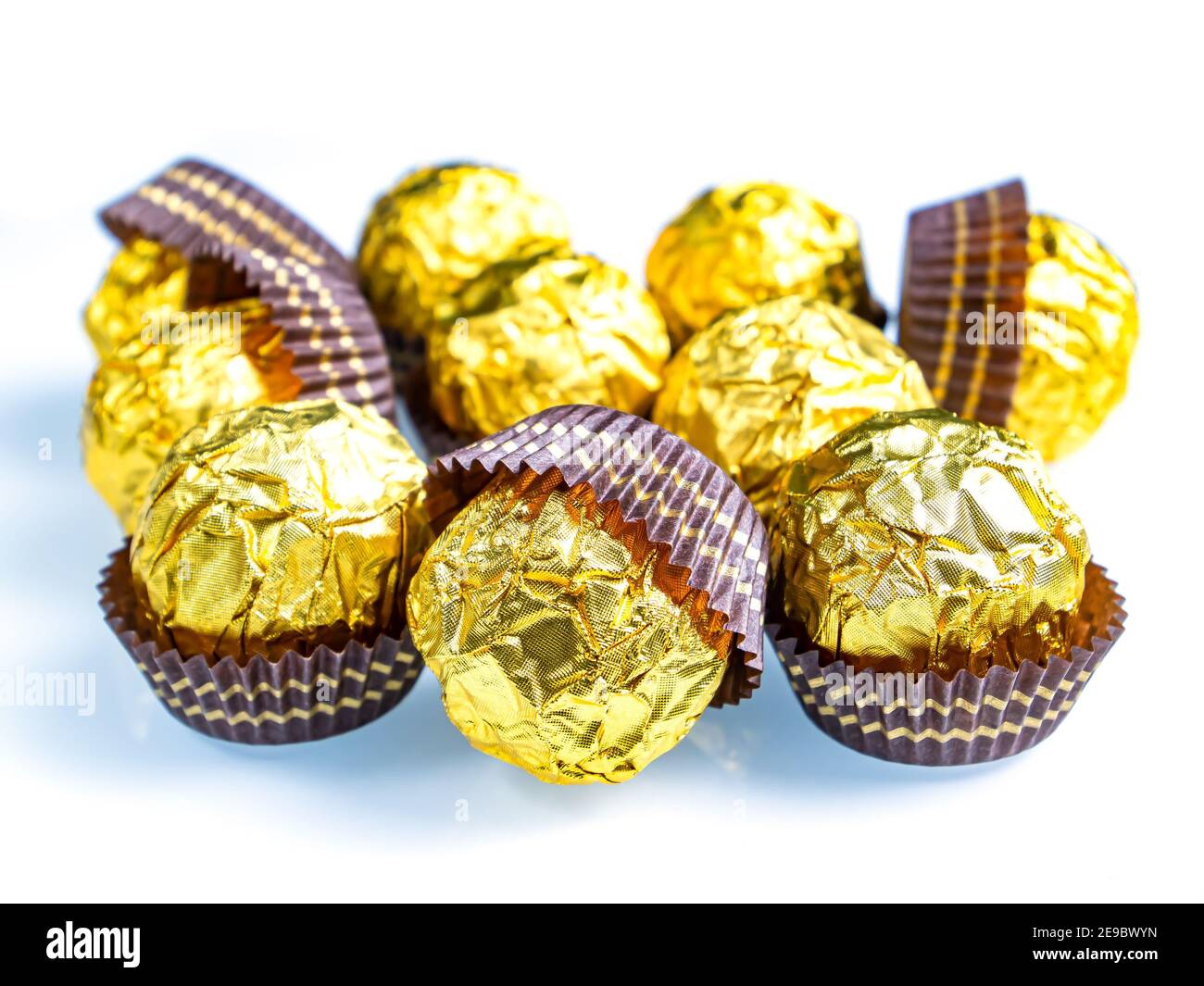 Round chocolate candies in a golden foil wrapper on a white background ...