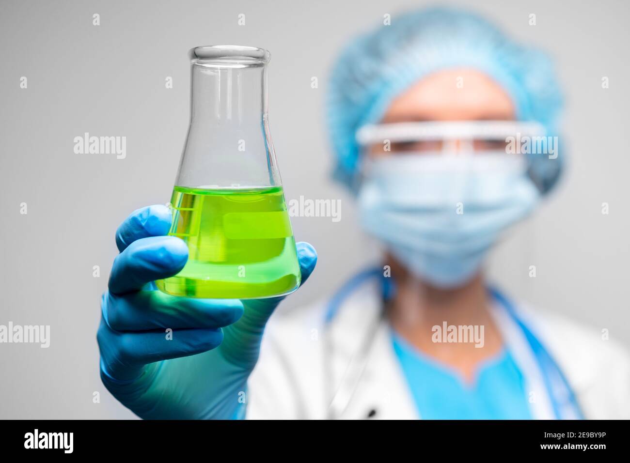 Woman scientist holding laboratory flask with chemical liquid, gray ...
