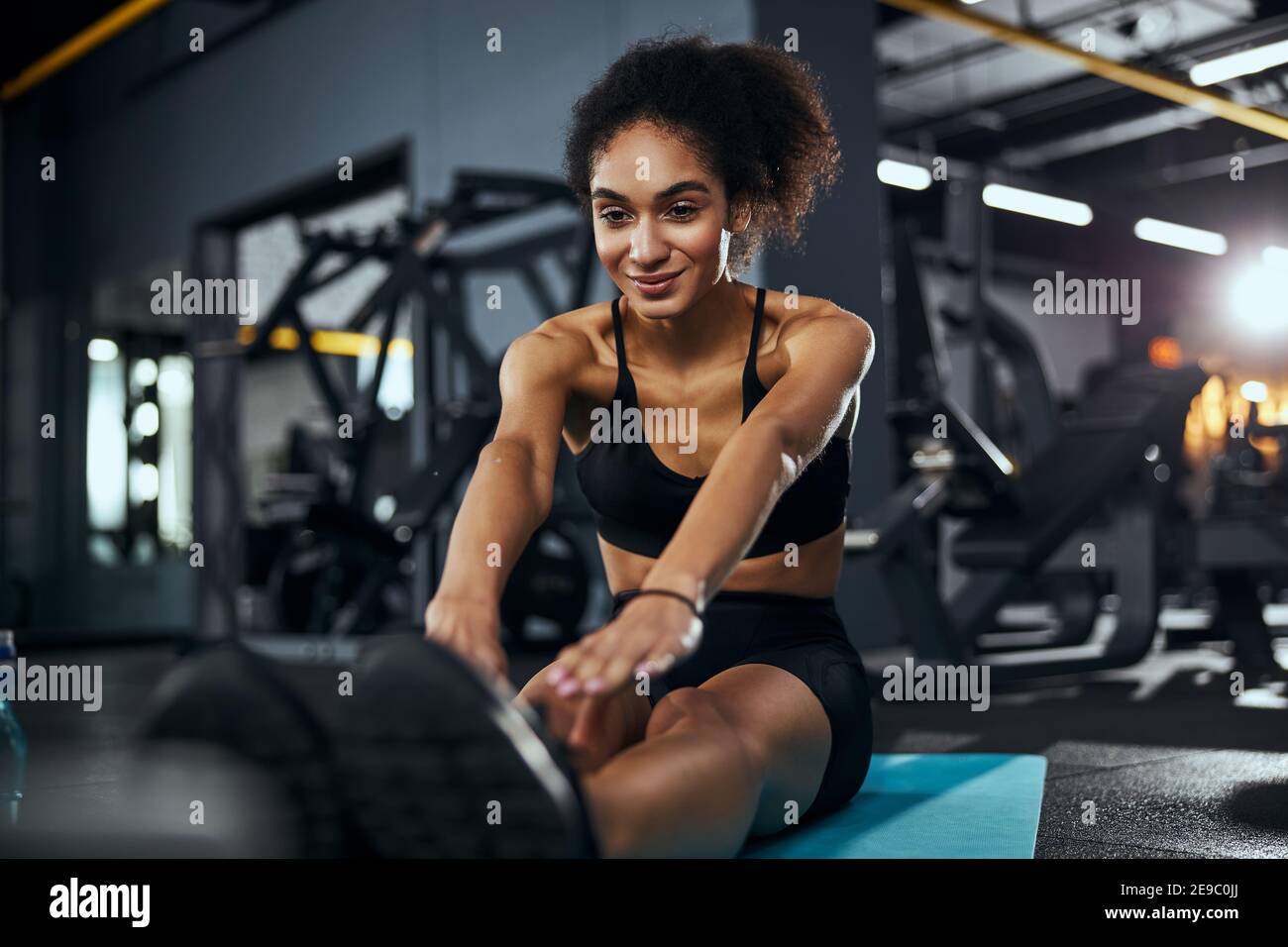 Young woman sitting on the mat and touching legs Stock Photo - Alamy