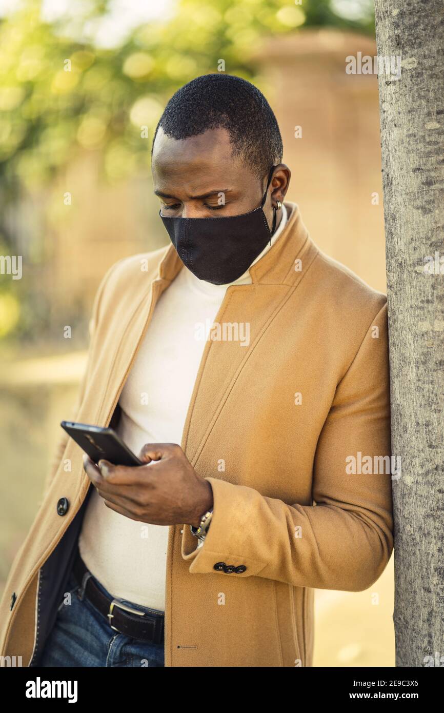 African male wearing a black face mask using his smartphone while ...
