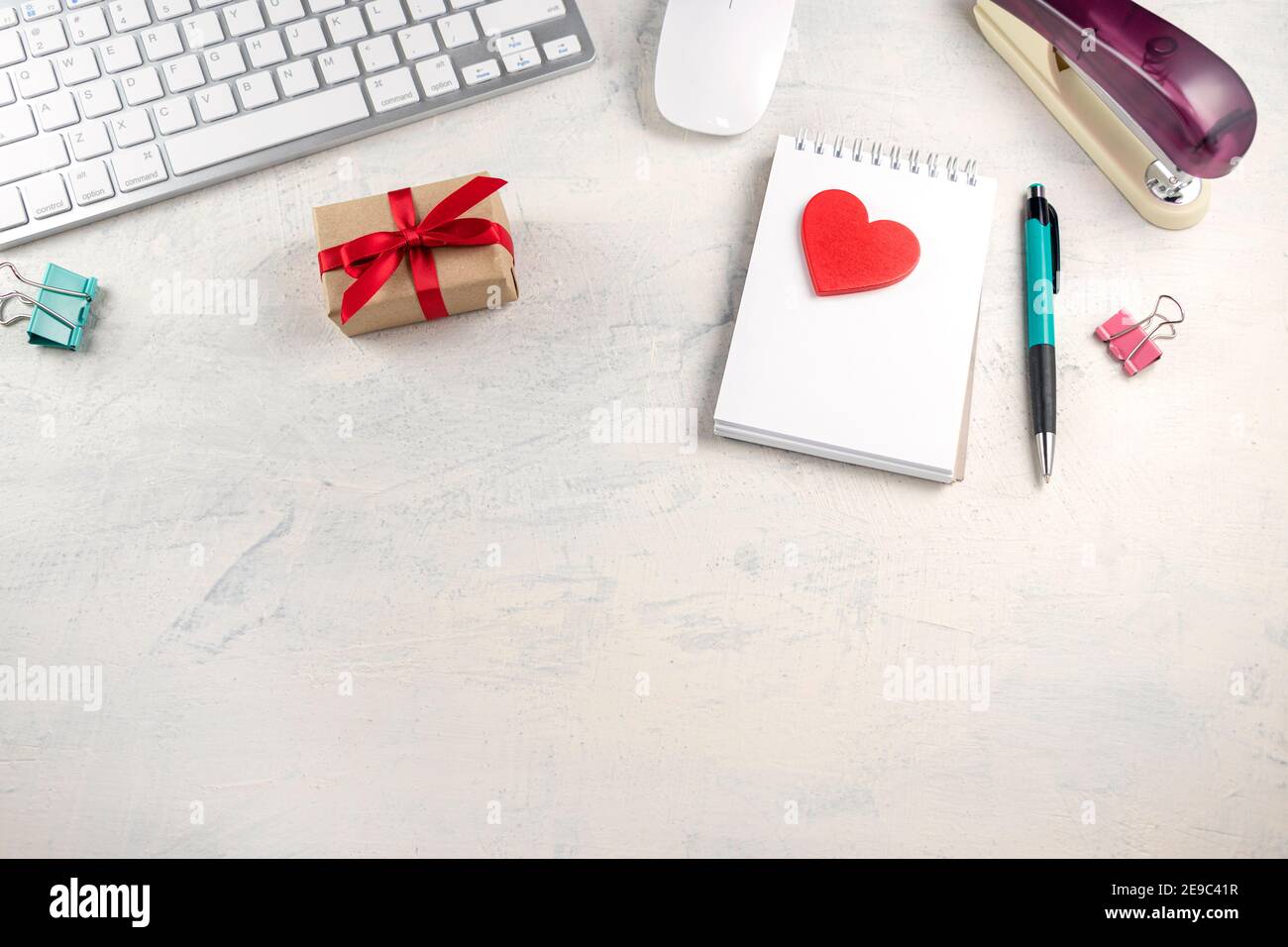 Red heart on notepad near keyboard, pen, mouse, stapler and gift with ...