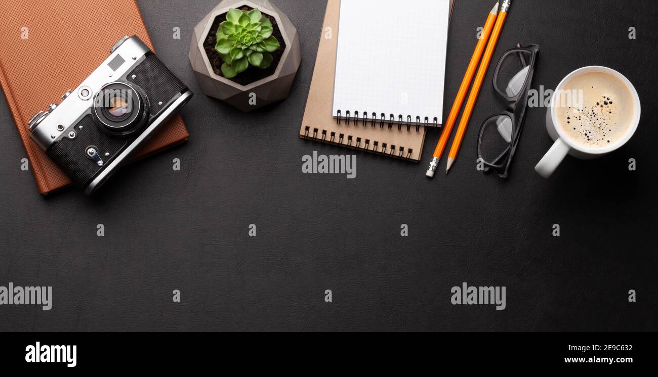 Office desk with supplies, photo camera and coffee over black leather ...