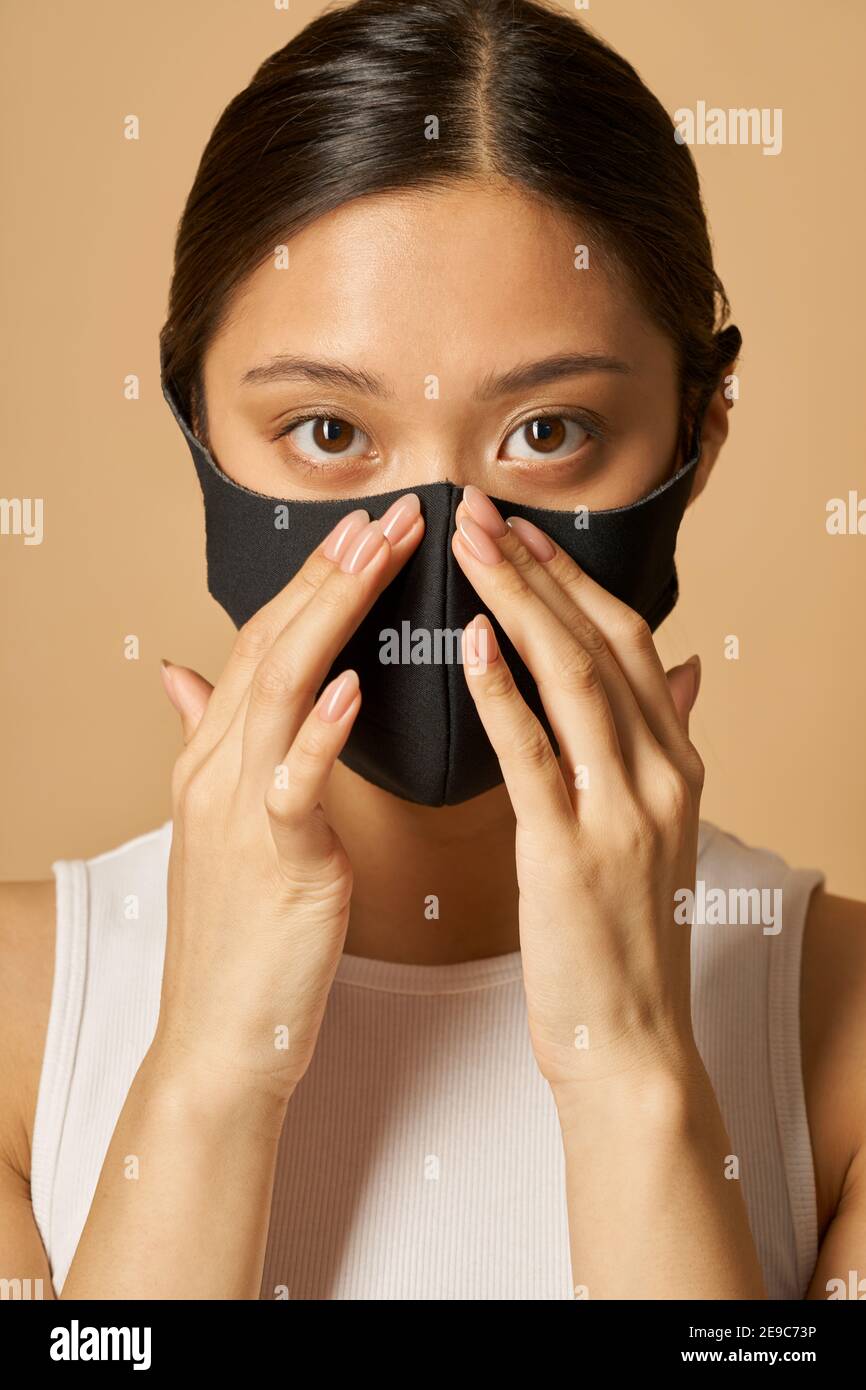Studio portrait of young woman putting on black facial mask, looking at ...