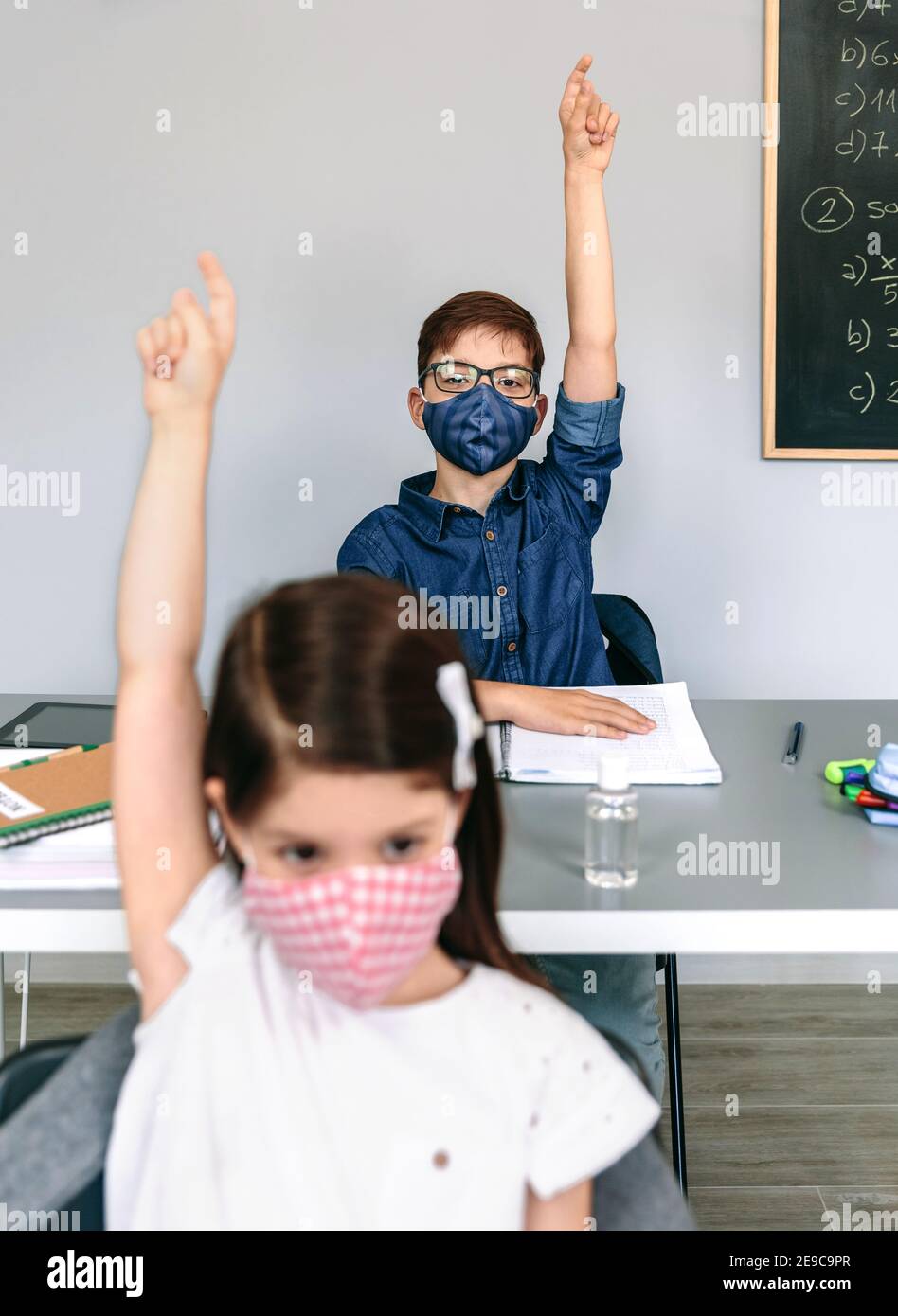 Students with masks raising hands at school Stock Photo - Alamy