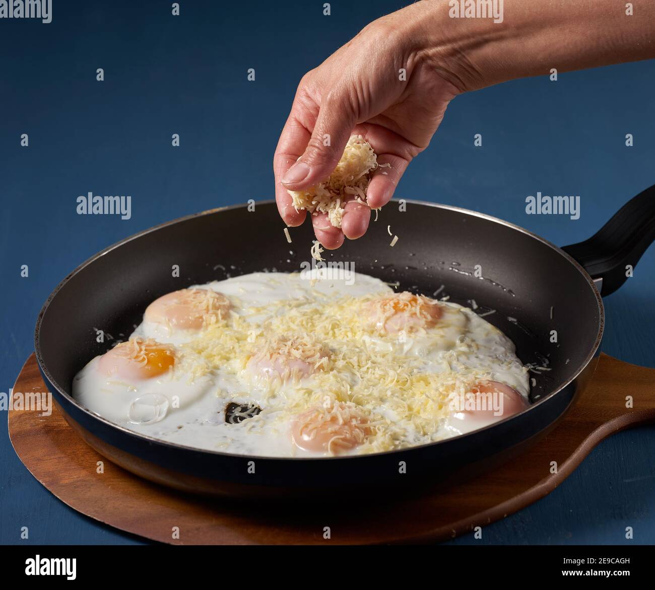Woman sprinkling grated cheddar cheese over frying eggs in the pan ...