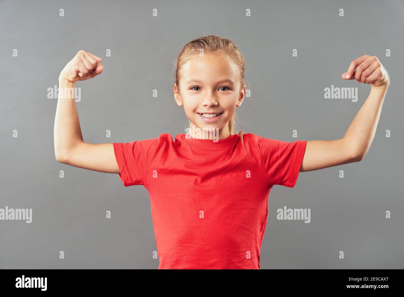 Adorable female child in red shirt showing her arm muscles and smiling ... Adorable female child in red shirt showing her arm muscles and smiling ...