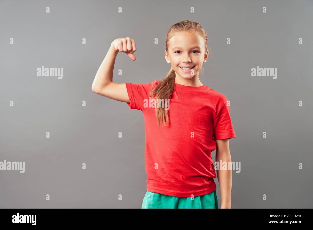Adorable female child showing her arm muscles and smiling while ... Adorable female child showing her arm muscles and smiling while ...