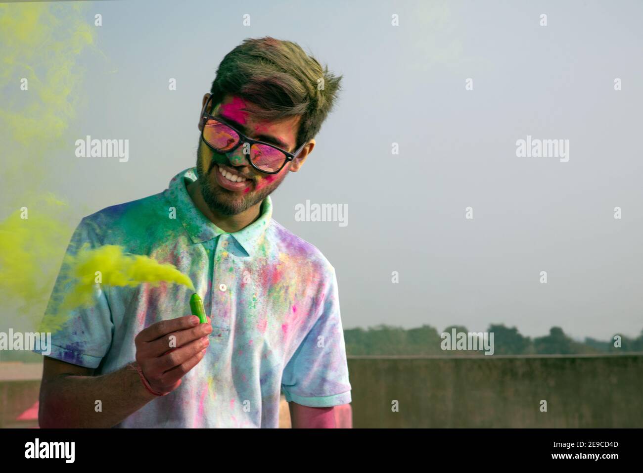 A HAPPY YOUNG MAN WITH GULAL ALL OVER HIM HOLDING COLOUR SMOKE BOMB ...