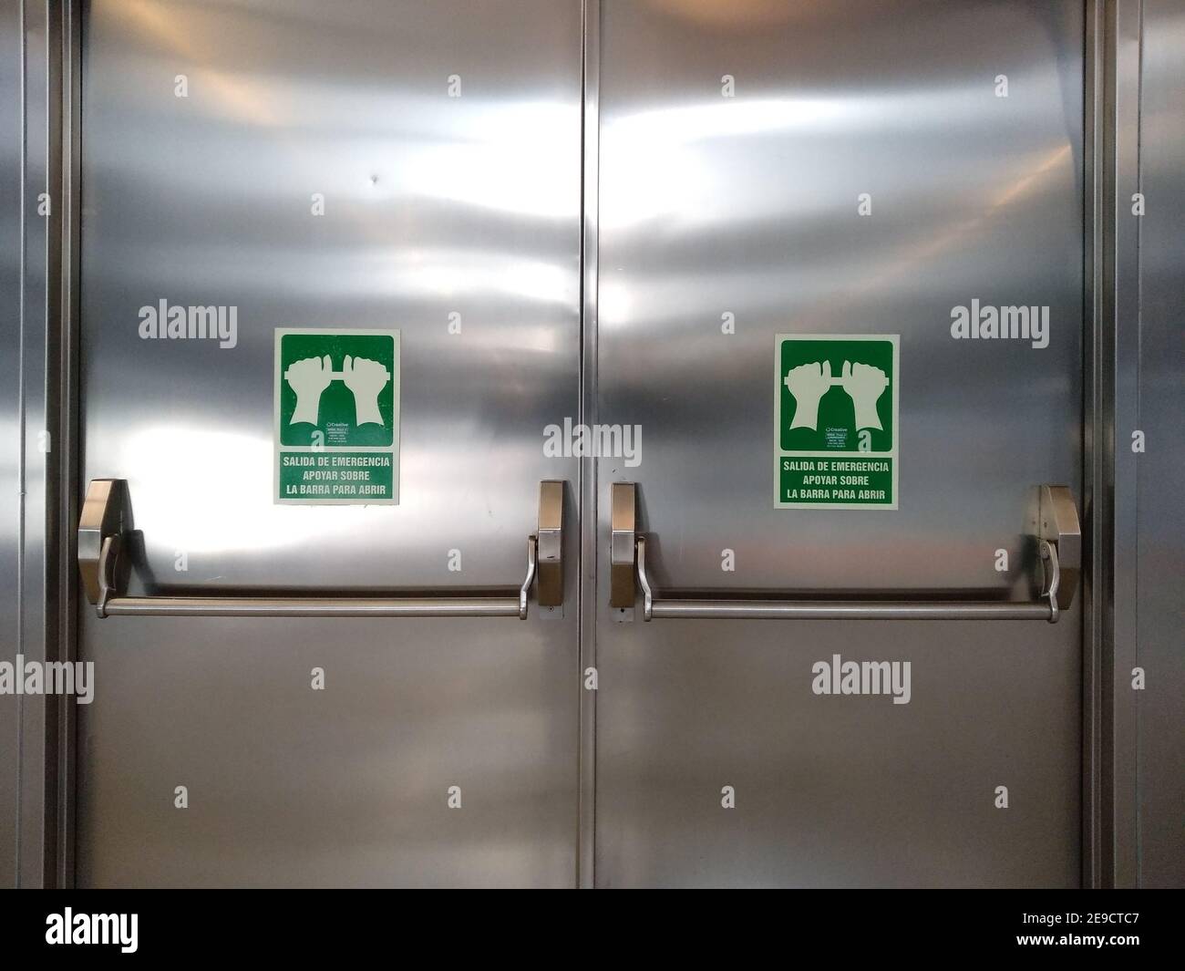 Closeup of a metal door with a green emergency exit sign in Spanish ...