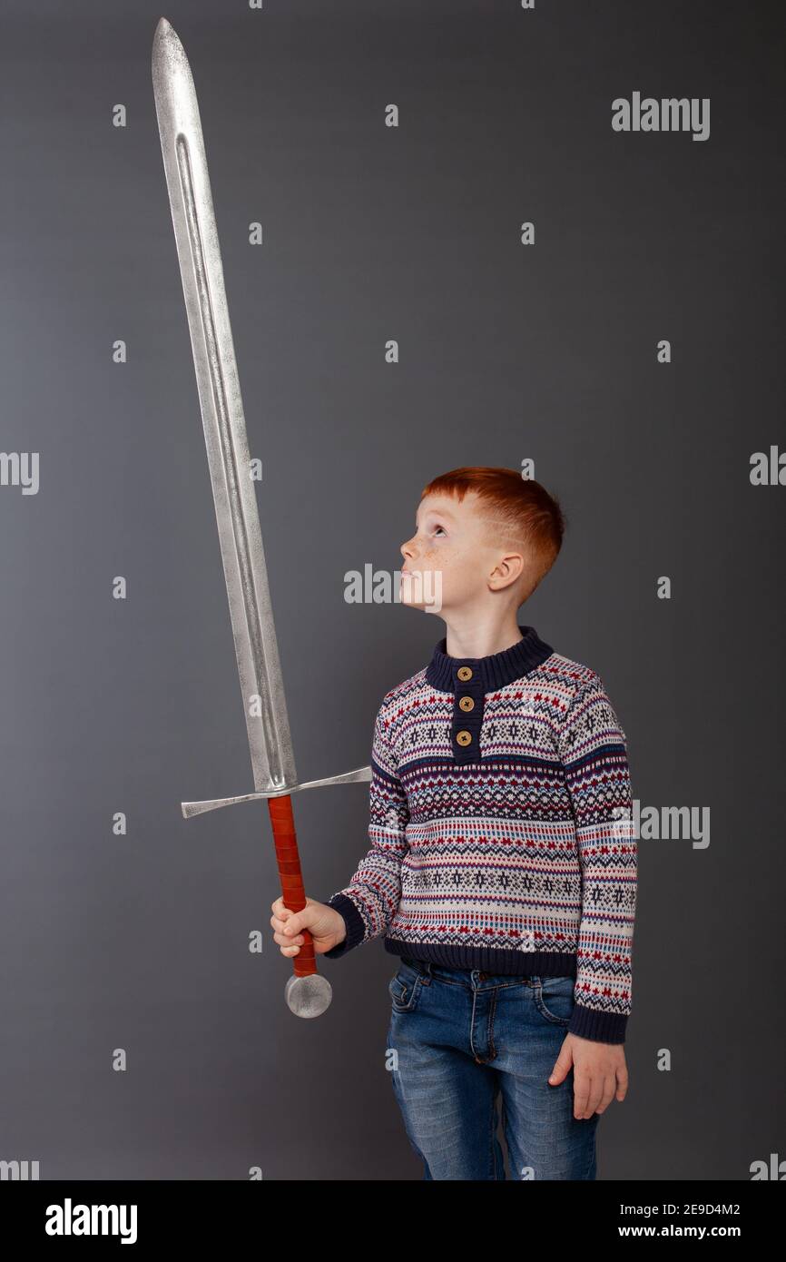 A little boy poses with a sword in a photo studio on a gray background ...