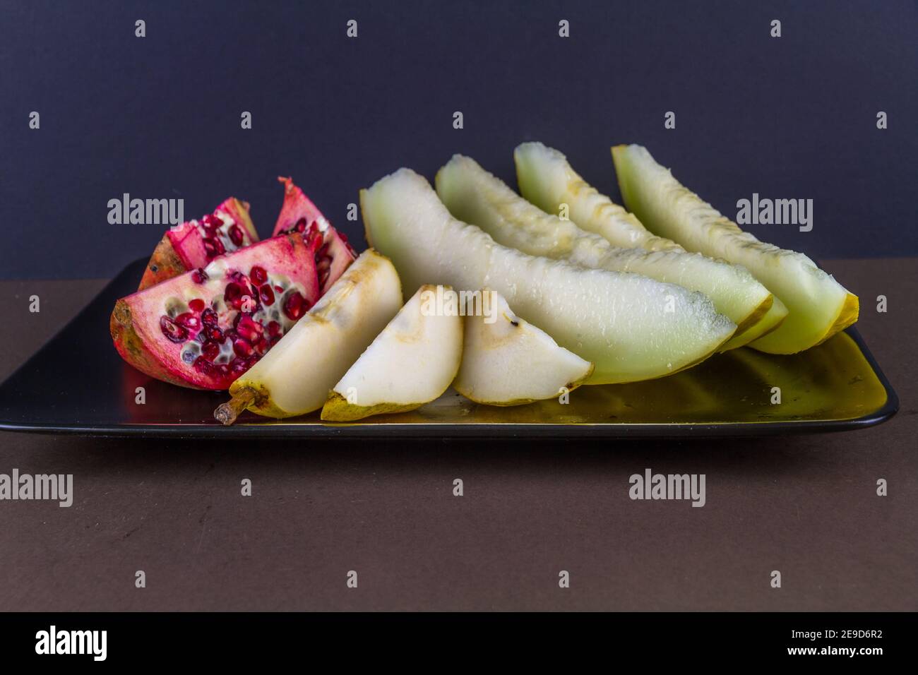 pomegranate melon and pear sliced and arranged on plate landscape. dark ...