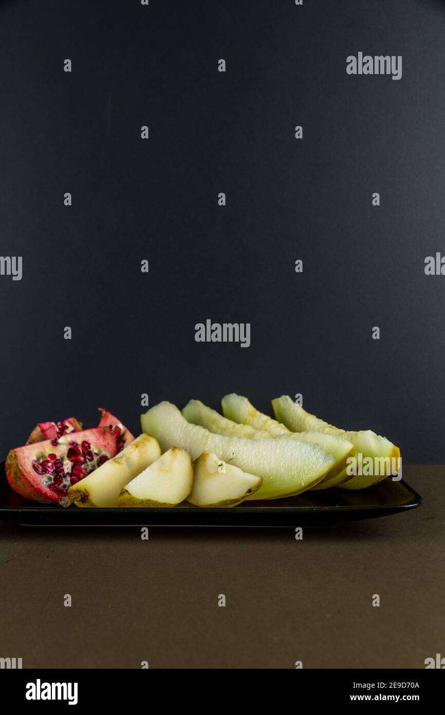 pomegranate melon and pear sliced and arranged on plate. dark ...