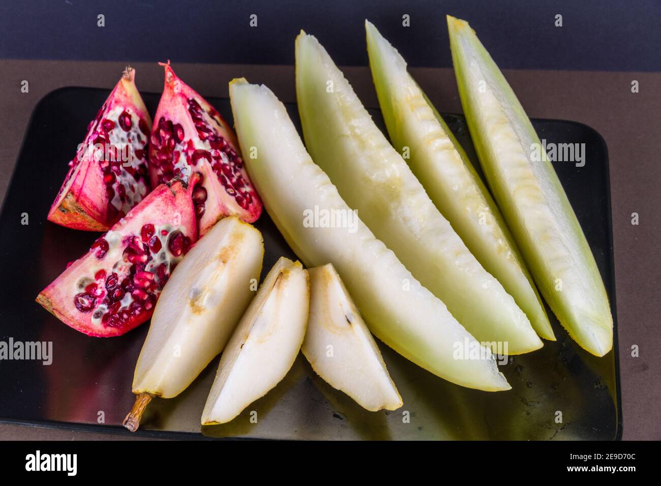 pomegranate melon and pear sliced and arranged on plate. dark ...