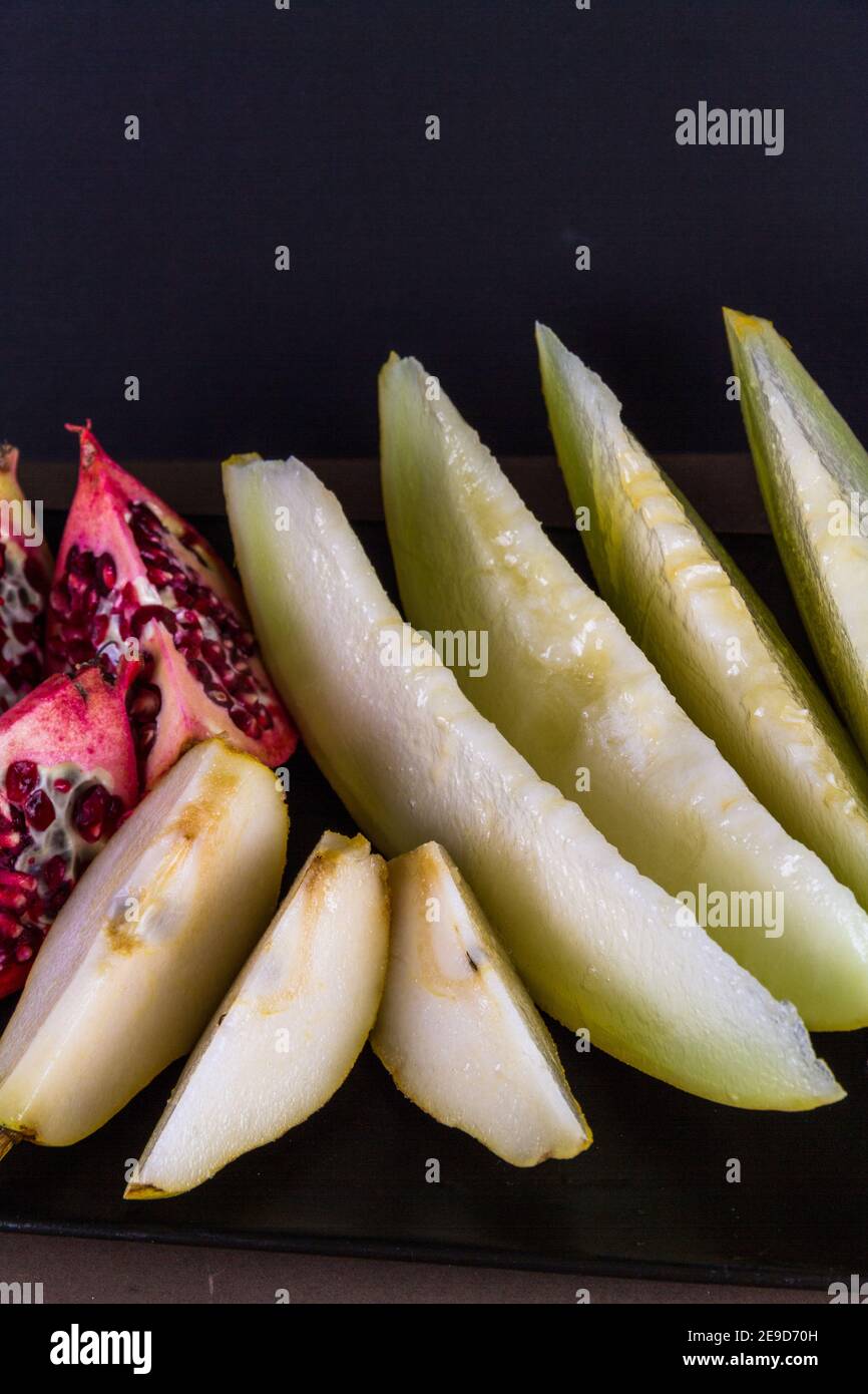 pomegranate melon and pear sliced and arranged on plate. dark ...